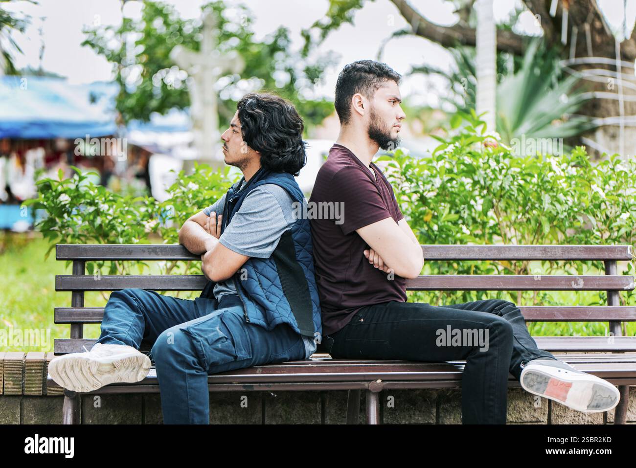 Two friends arguing on a park bench. Two angry friends sitting on a ...