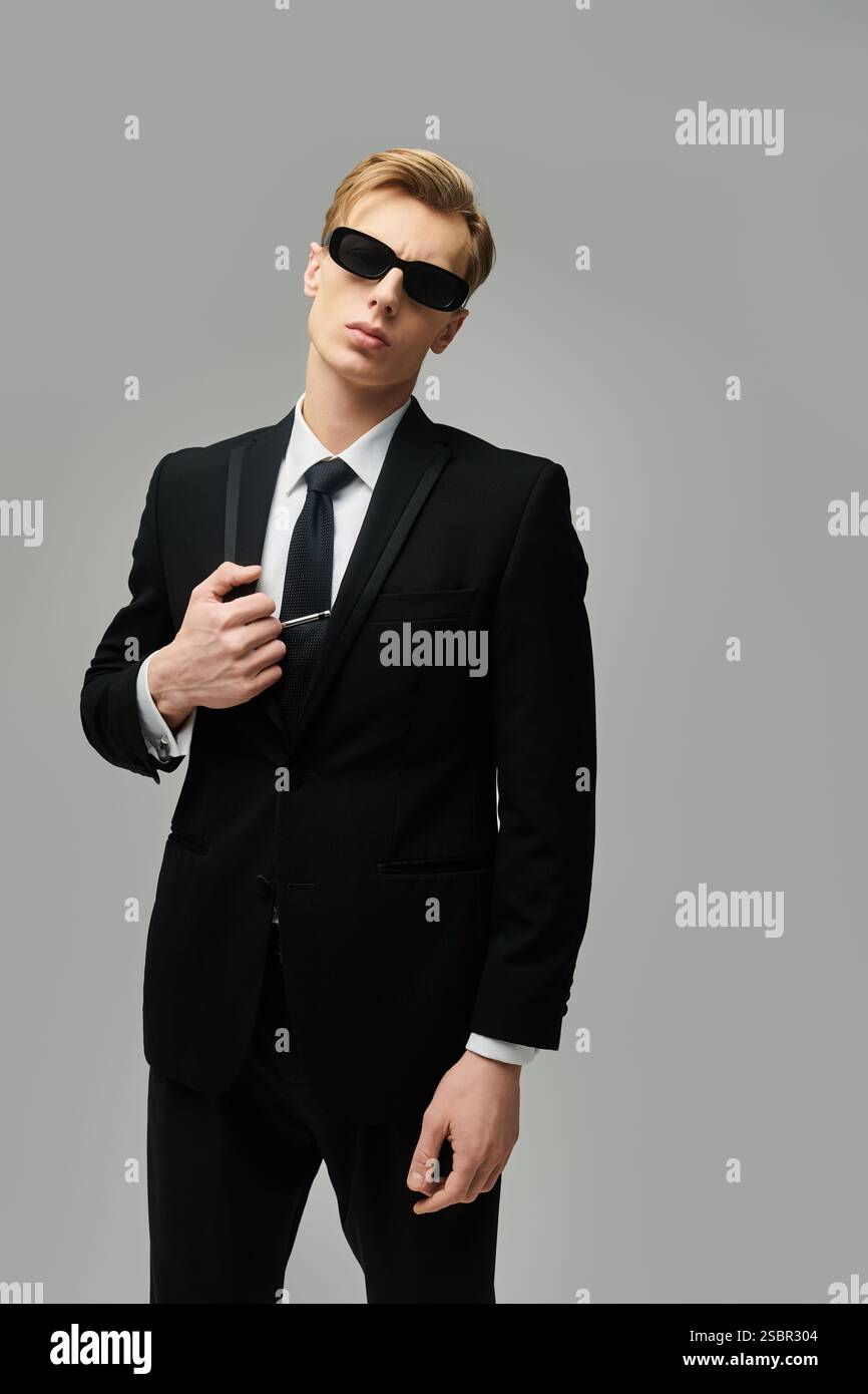 A young handsome man dressed in a sharp black suit and sunglasses ...