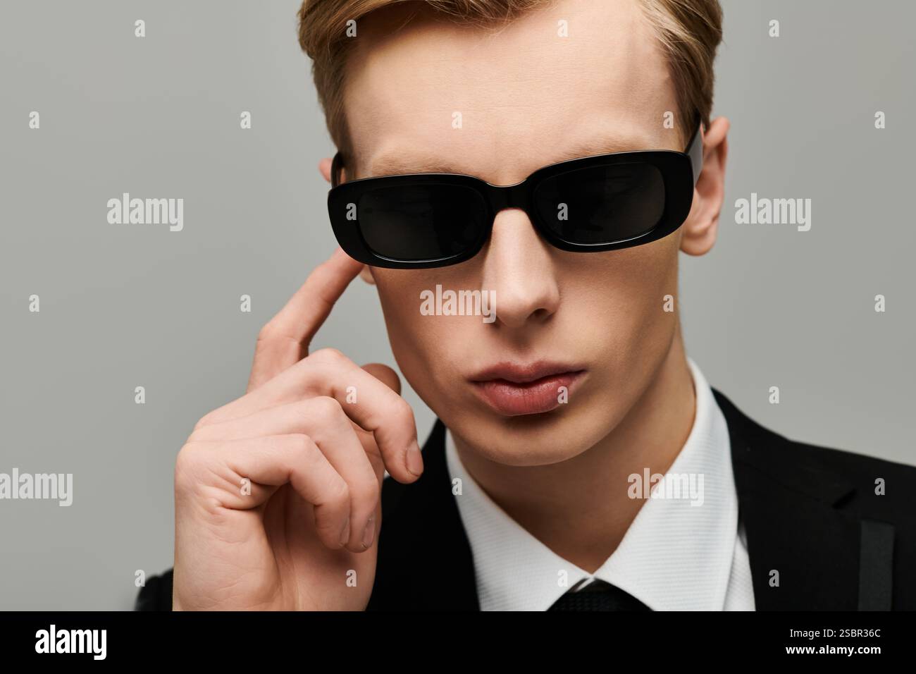 Confident young man adjusts his sunglasses while sporting a sharp suit ...