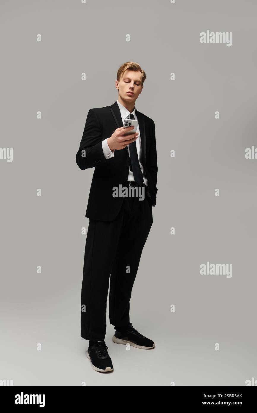 Confident young man dressed in a sleek suit engages with his smartphone ...