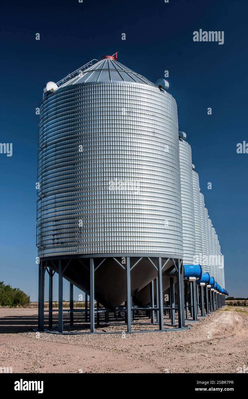 A row of silos are lined up in a field. The silos are tall and made of ...