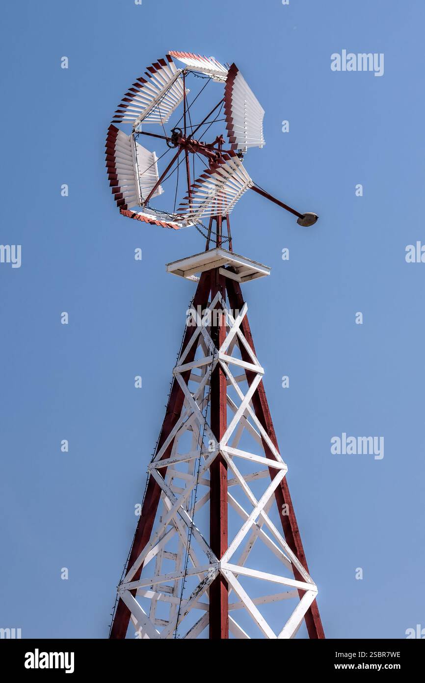 A windmill is on top of a tall pole. The pole is white and red. The windmill is spinning Stock ...