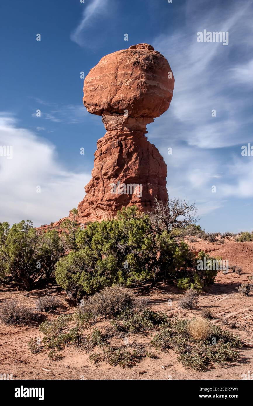 A large rock with a pointy top. The rock is surrounded by bushes. The ...