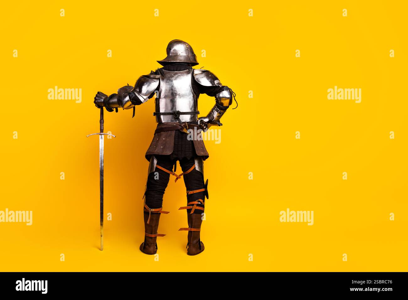 Rear view of a knight in full suit of armor holding a sword against a ...