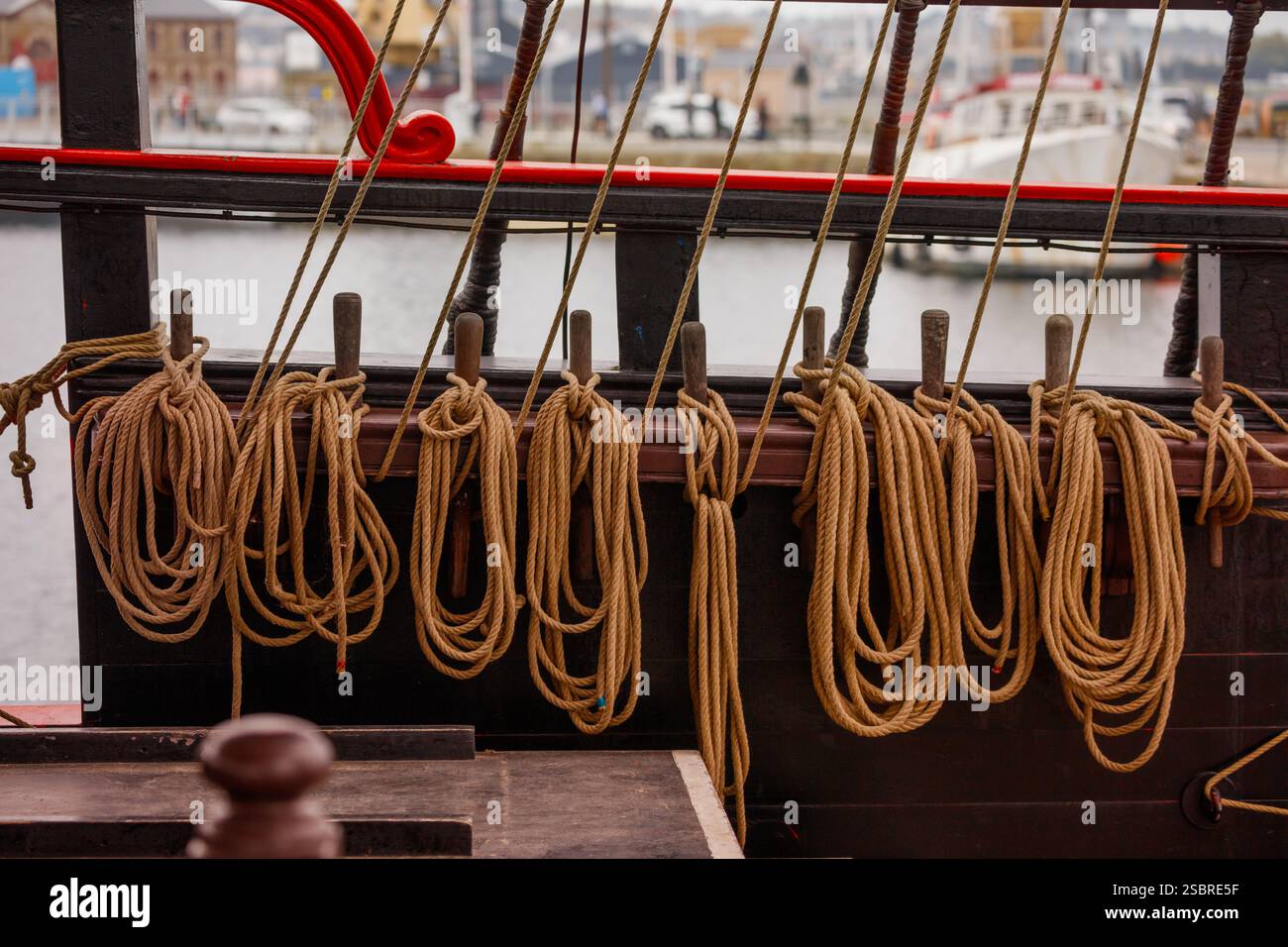 Coils of thick ropes are hanging from wooden pins aboard an old sailing ...