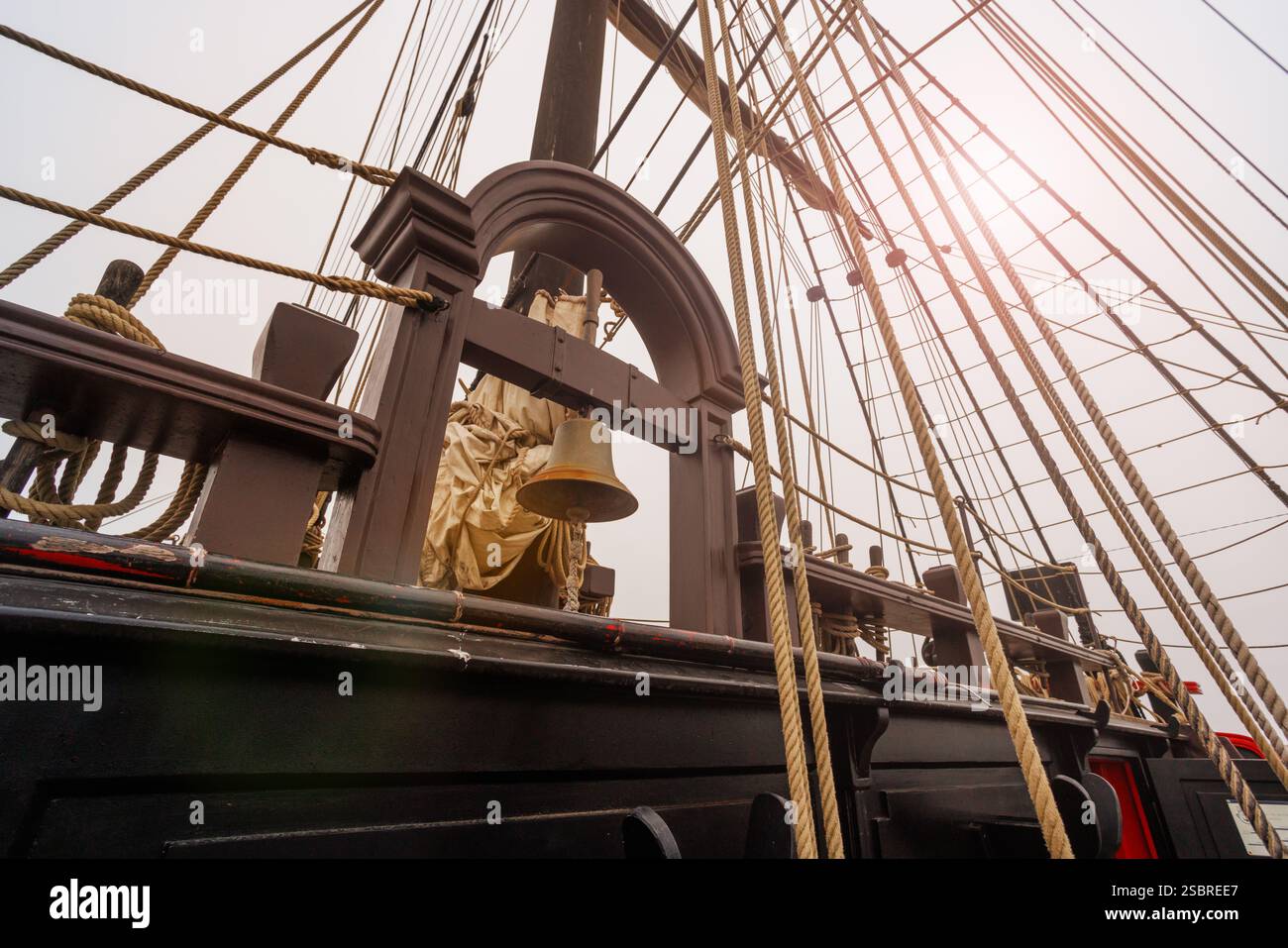 Rigging and bell of a historic sailing vessel, highlighted by rays of ...