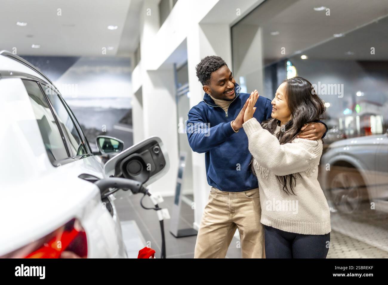 Happy multiethnic couple celebrating their new electric car purchase ...