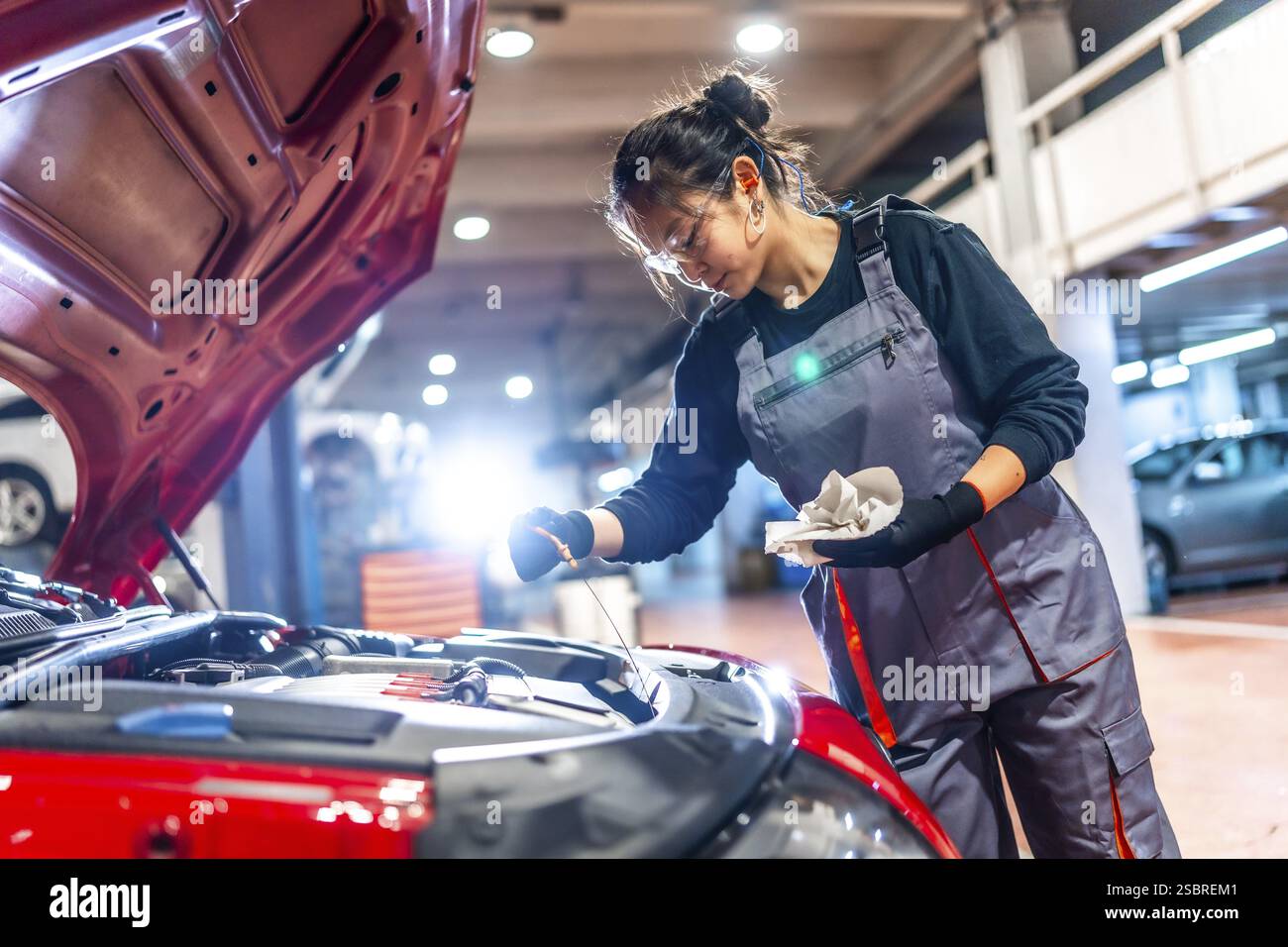 Young female mechanic wearing overalls and protective glasses is ...