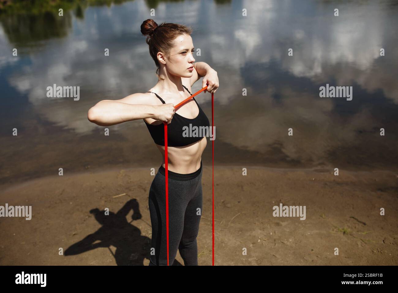 A focused woman exercises with a resistance band, casting a shadow on ...