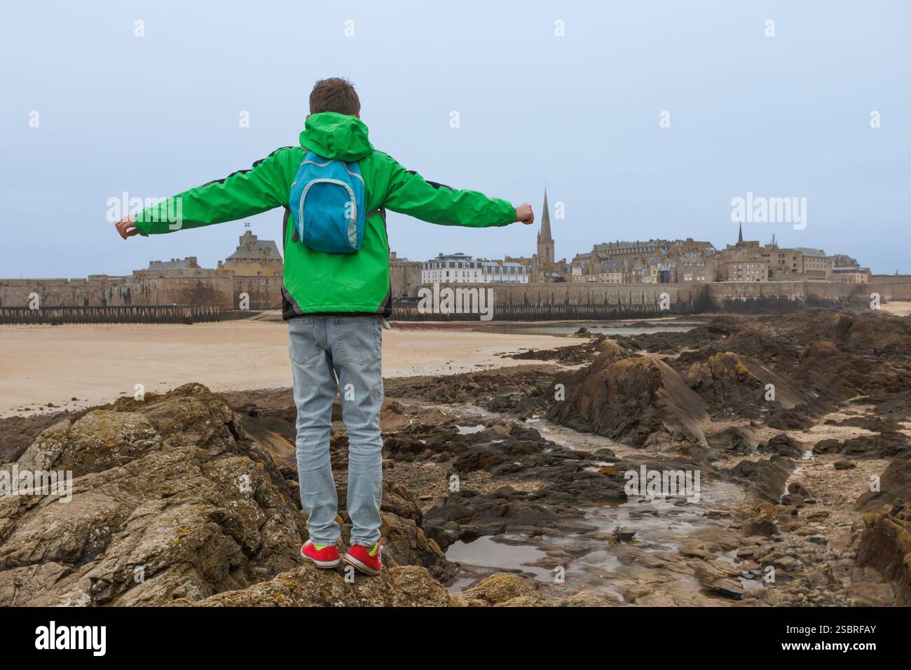 Explorer stands on rocks, facing the city's historic skyline Stock ...