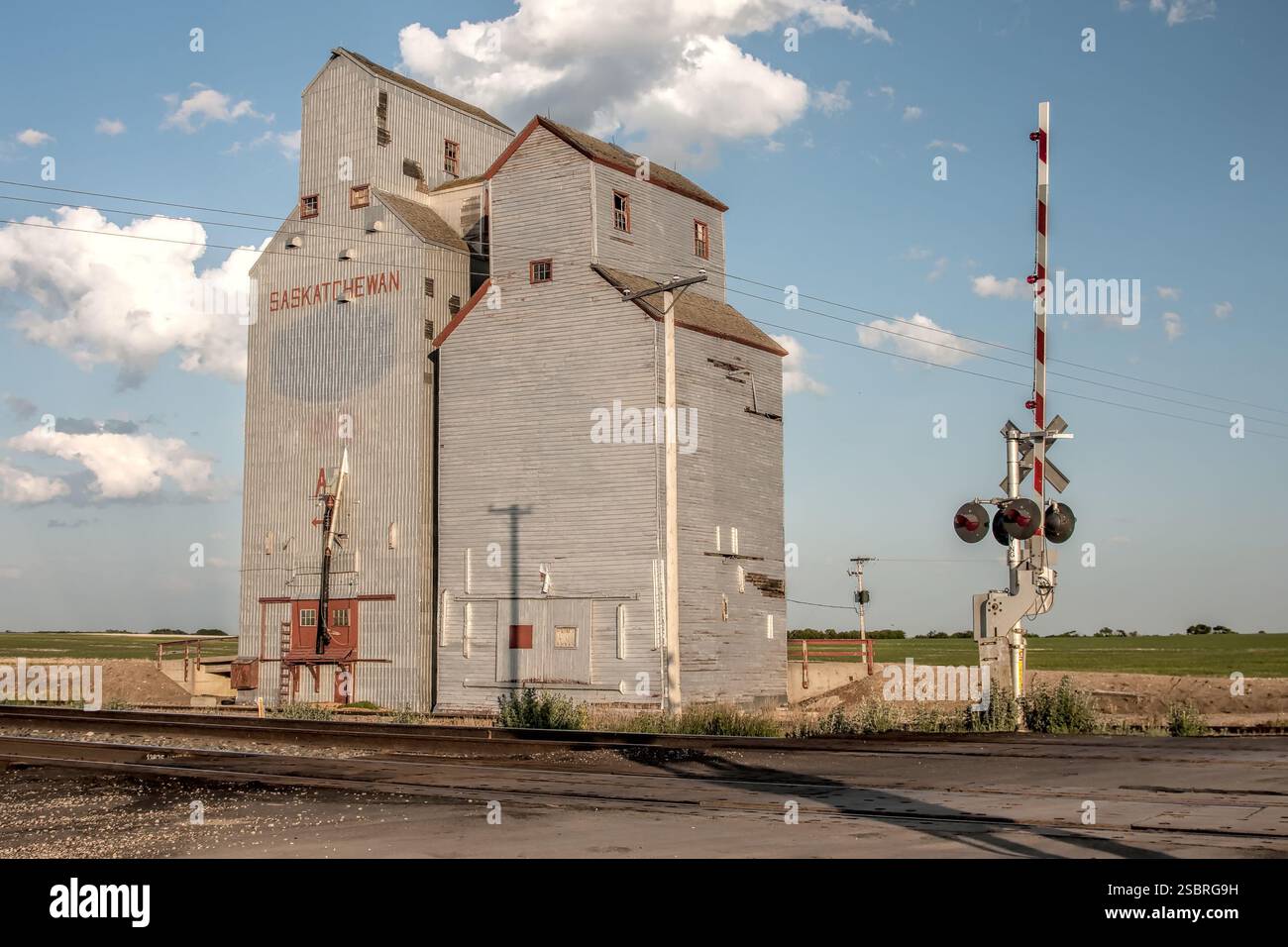 A grain silo is next to a railroad crossing. The silo is white and has ...
