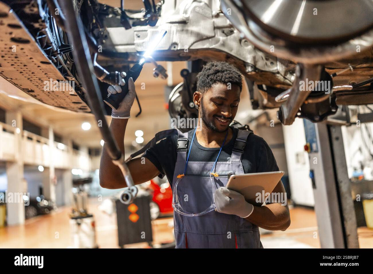 Young mechanic using a digital tablet while working on a car held up by ...
