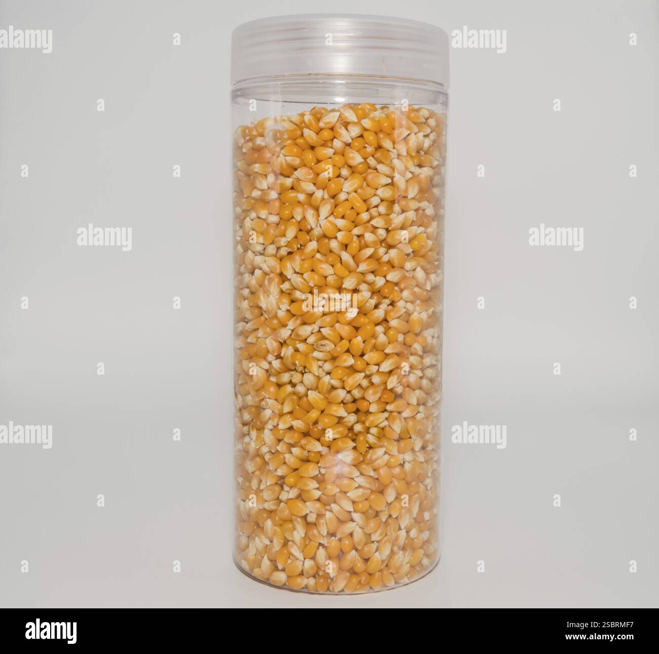 Clear container filled with yellow popcorn kernels on white background ...