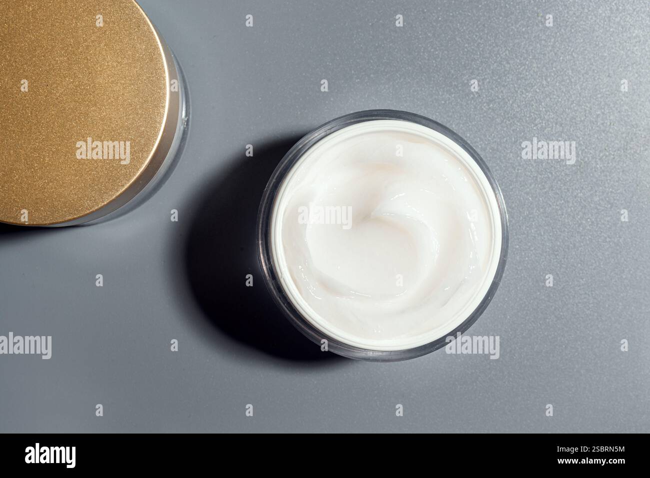 Open cream jar with golden lid on neutral grey background, top view ...