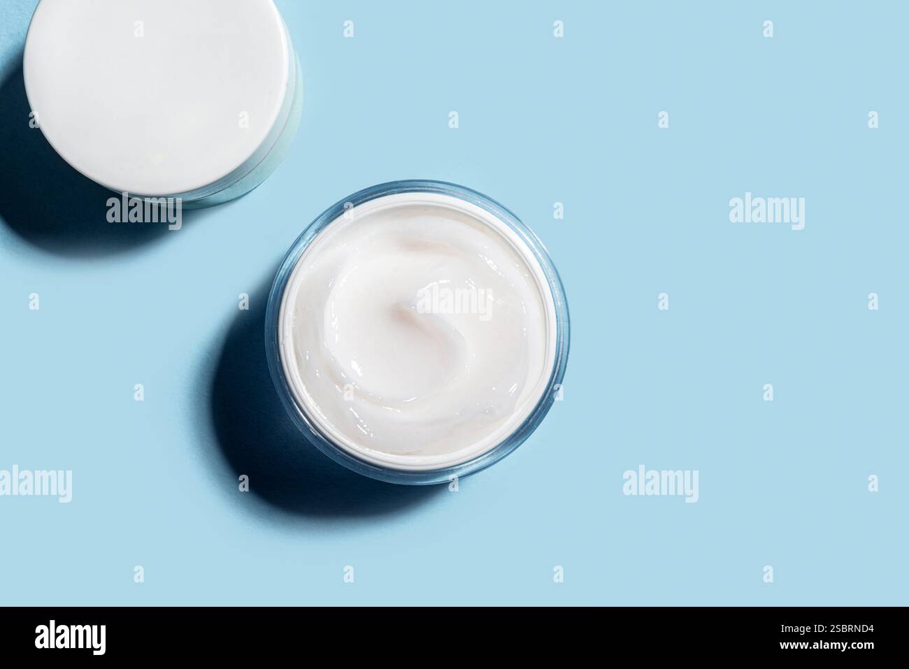 Open cosmetic cream jar on blue background, top view, copy space. Gel ...