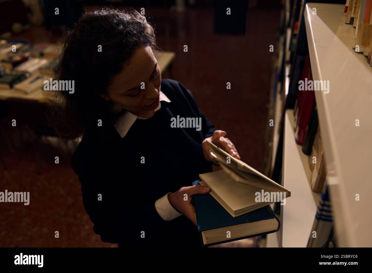 A woman is seen browsing and selecting books from shelves in a library ...
