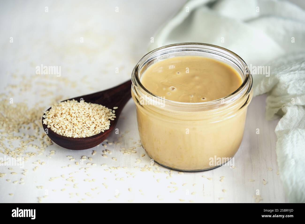 Top view of mason jar filled with tahini. Wooden spoon overflowing with ...
