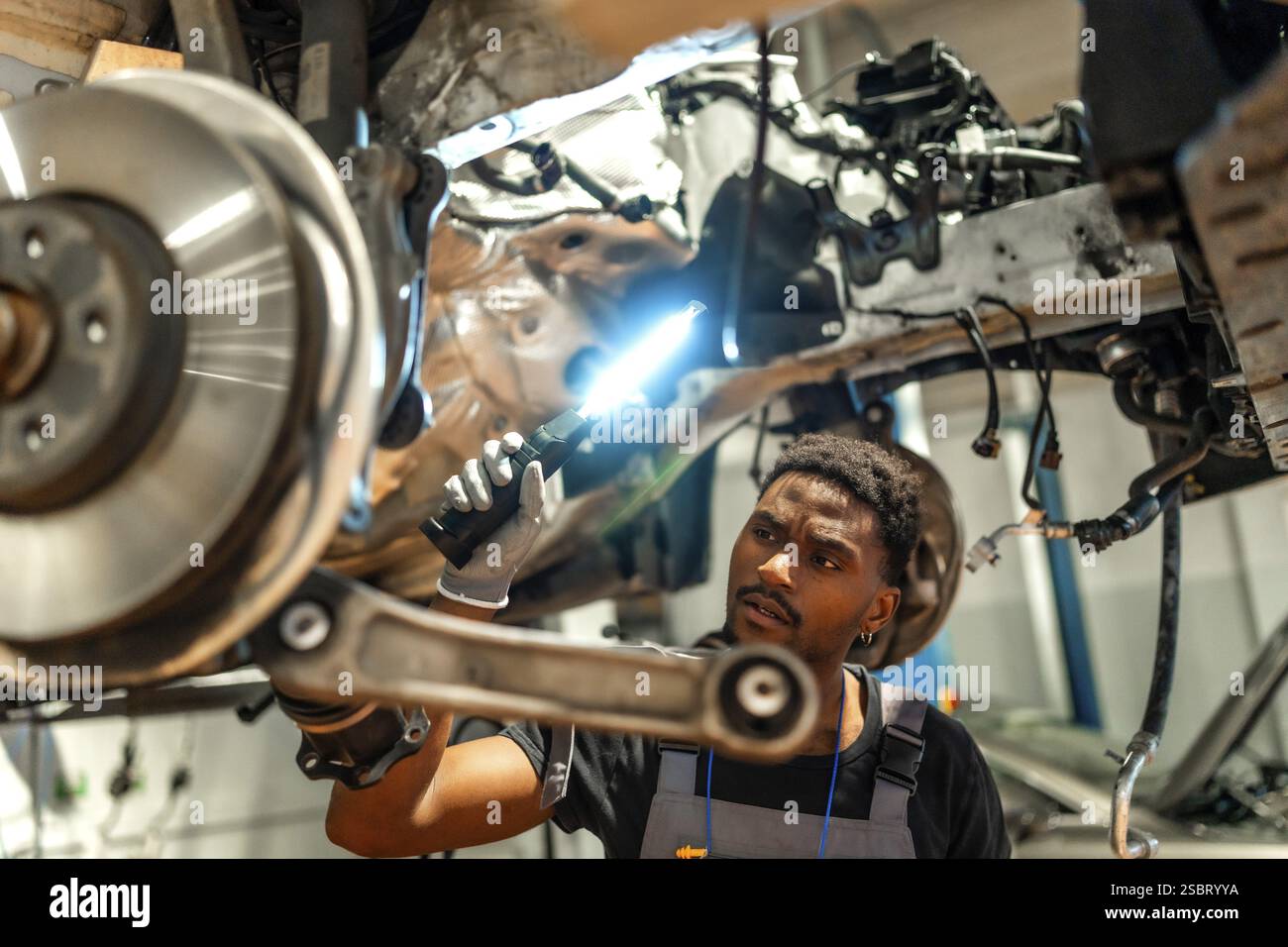 Young mechanic using flashlight inspecting car chassis and suspension ...