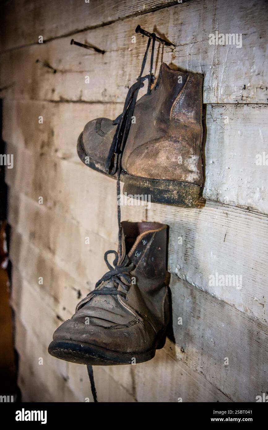 Two old shoes are hanging on a wall. One is a brown boot and the other ...