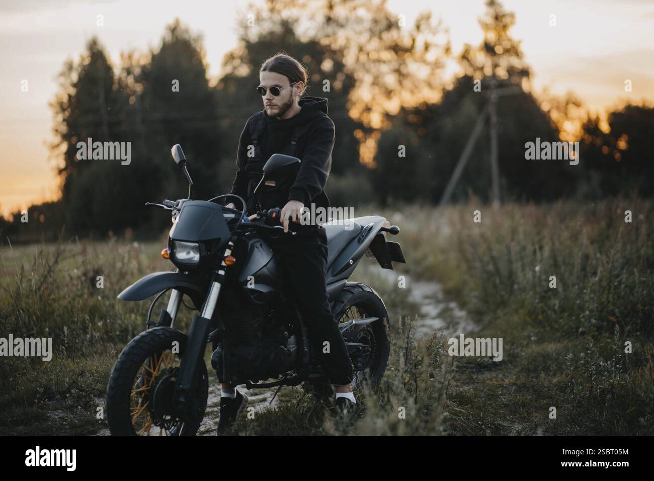 Man sits on a motorcycle on a nature path at sunset, embodying ...