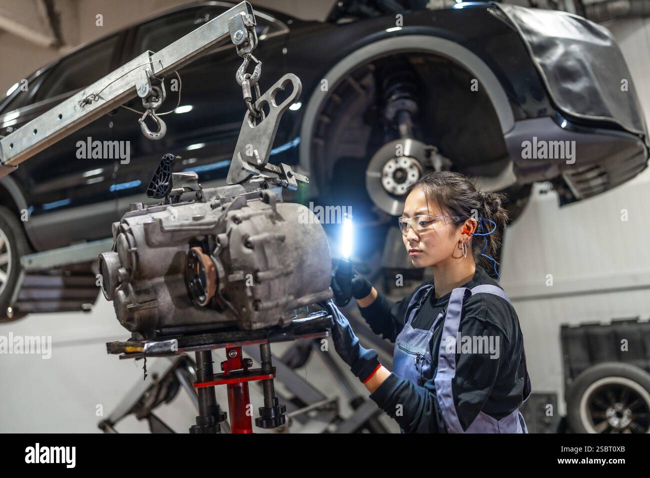 Young woman mechanic using flashlight, inspecting gearbox in car ...