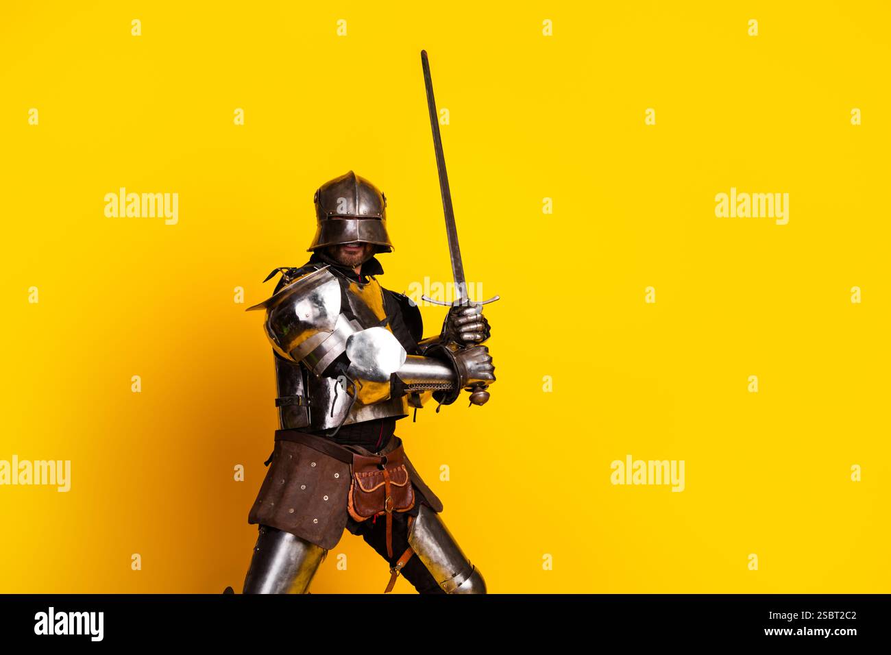 Knight in medieval armor posing with a sword against a bold yellow ...