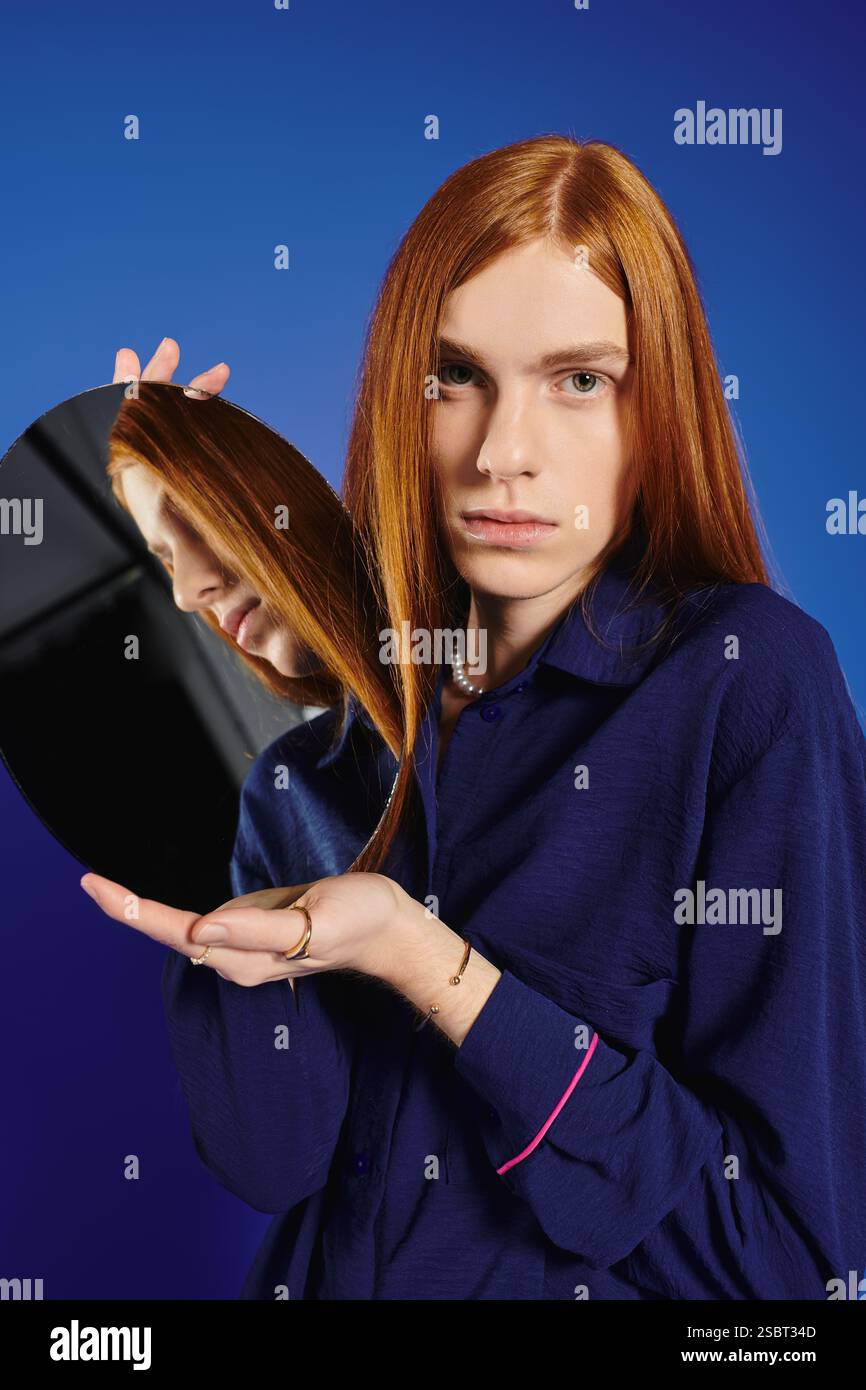 A stylish young person with long red hair checks their reflection in a ...