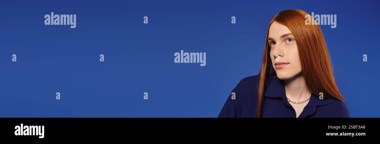 A young man with striking long red hair poses confidently in stylish ...