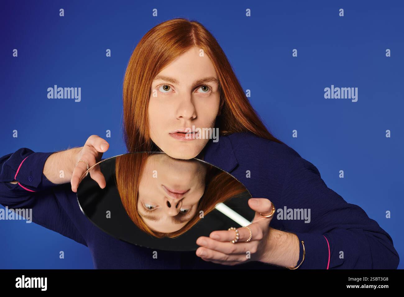 Man with long red hair engages with a mirror, reflecting his stylish ...
