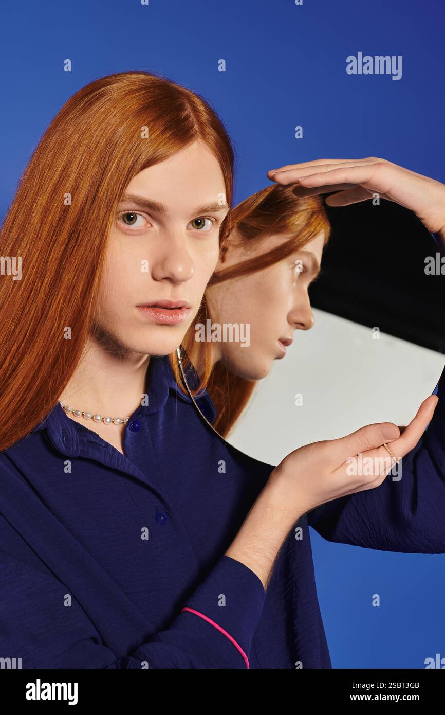 A young queer man with long red hair poses with a mirror, exploring ...