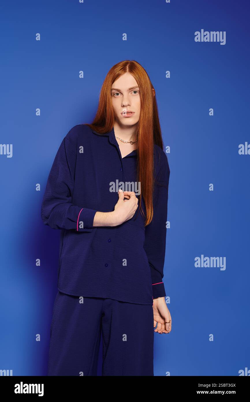 A stylish young man with striking red hair poses against a vibrant blue ...