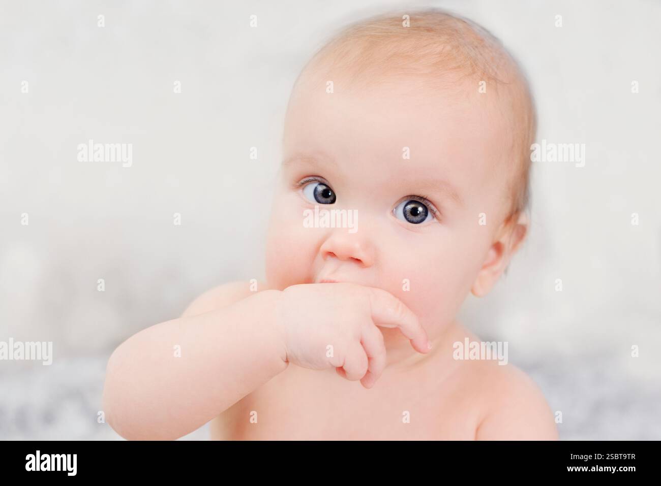 Close-up of baby with blue eyes and fair skin sucking their thumb and ...