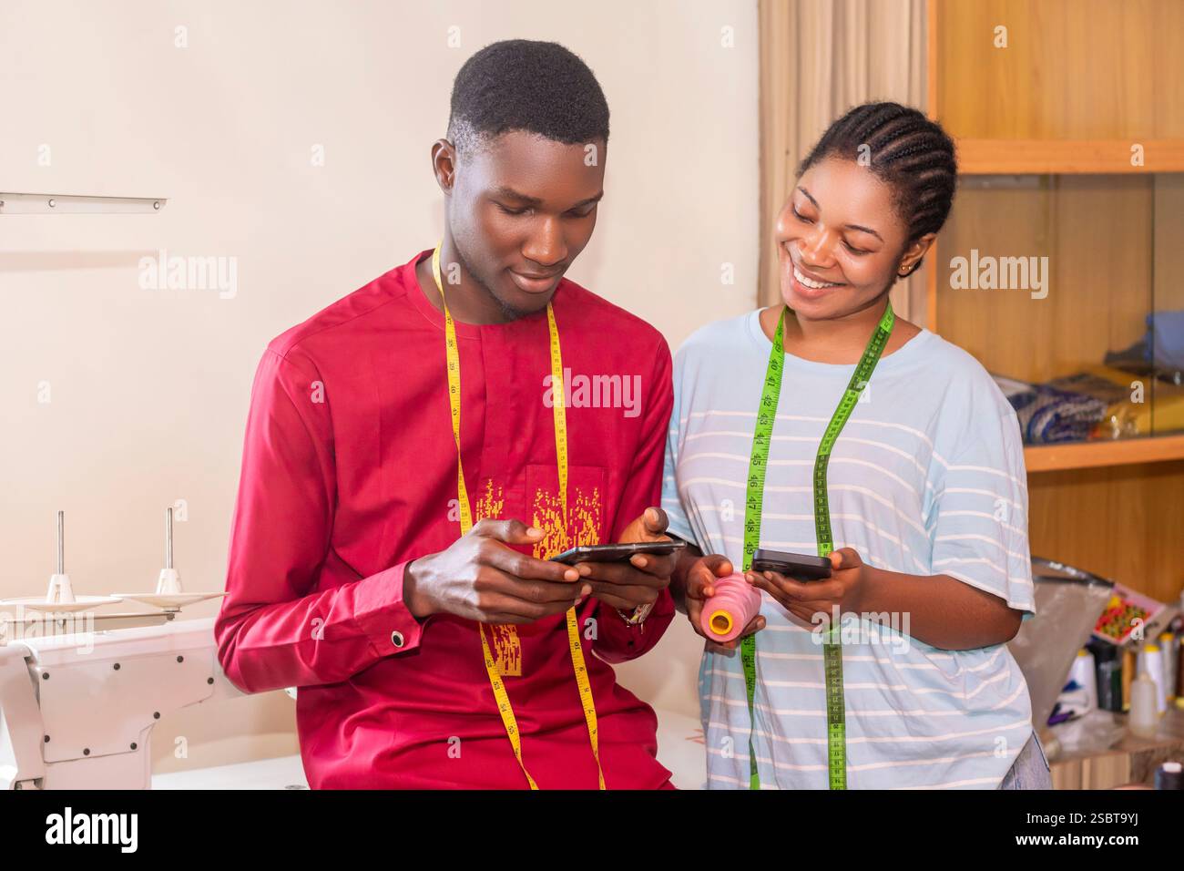 Young female trainee learning craft from a male tailor using cellphone ...