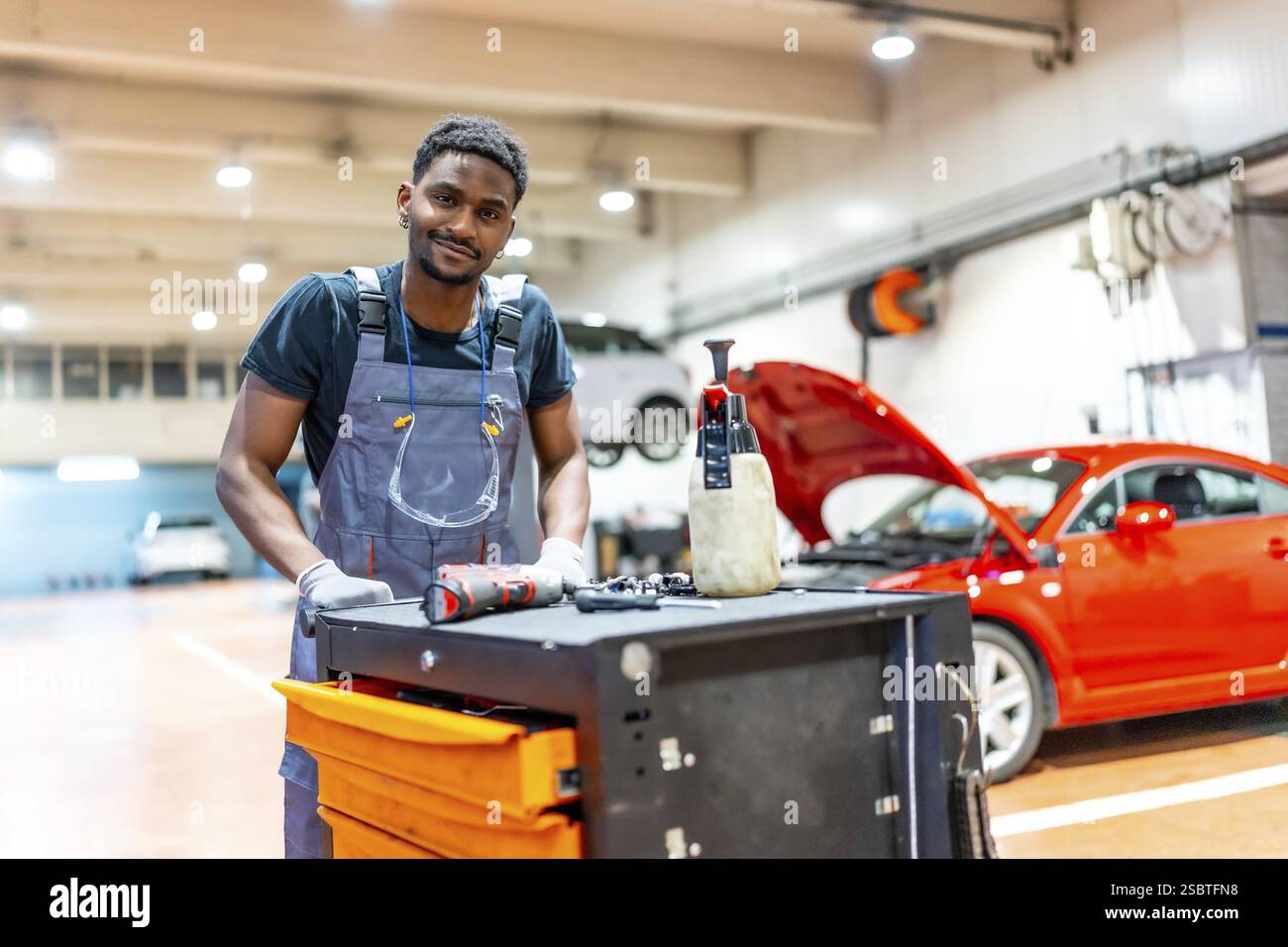 Young smiling african car mechanic pushing a tool trolley filled with ...