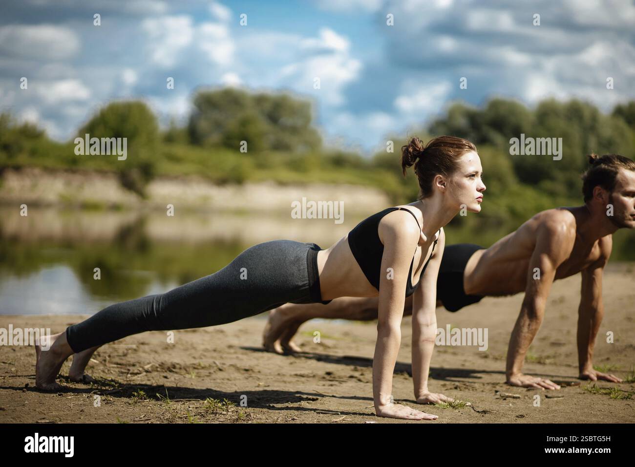 Man and woman holding plank positions on a lakeside sand area under a ...