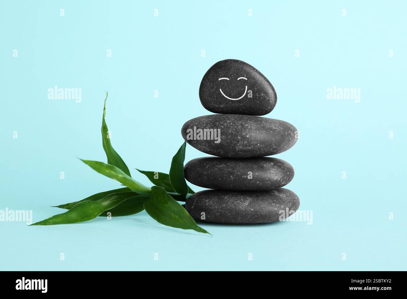 Stack of rocks with drawn smiley face on light blue background. Harmony ...