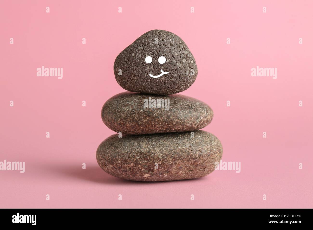 Stack of rocks with drawn smiley face on light pink background. Harmony ...