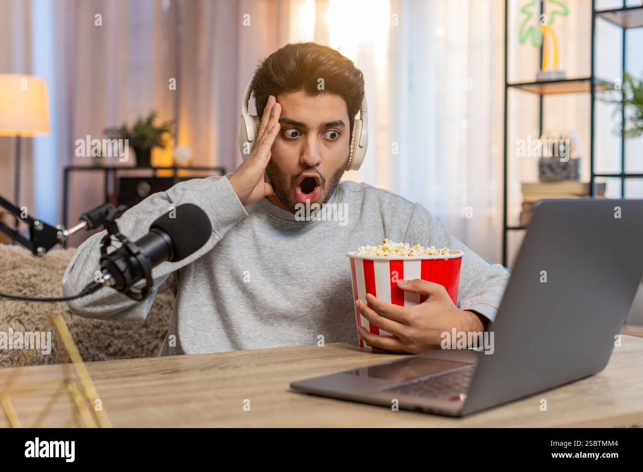 Young Indian man streams online laptop, watches football match, comments for subscribers, eats ...