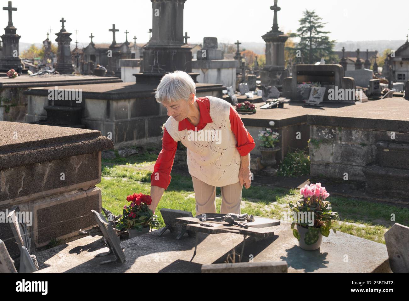 A grey-haired old woman lays flowers on her husband's grave in a ...