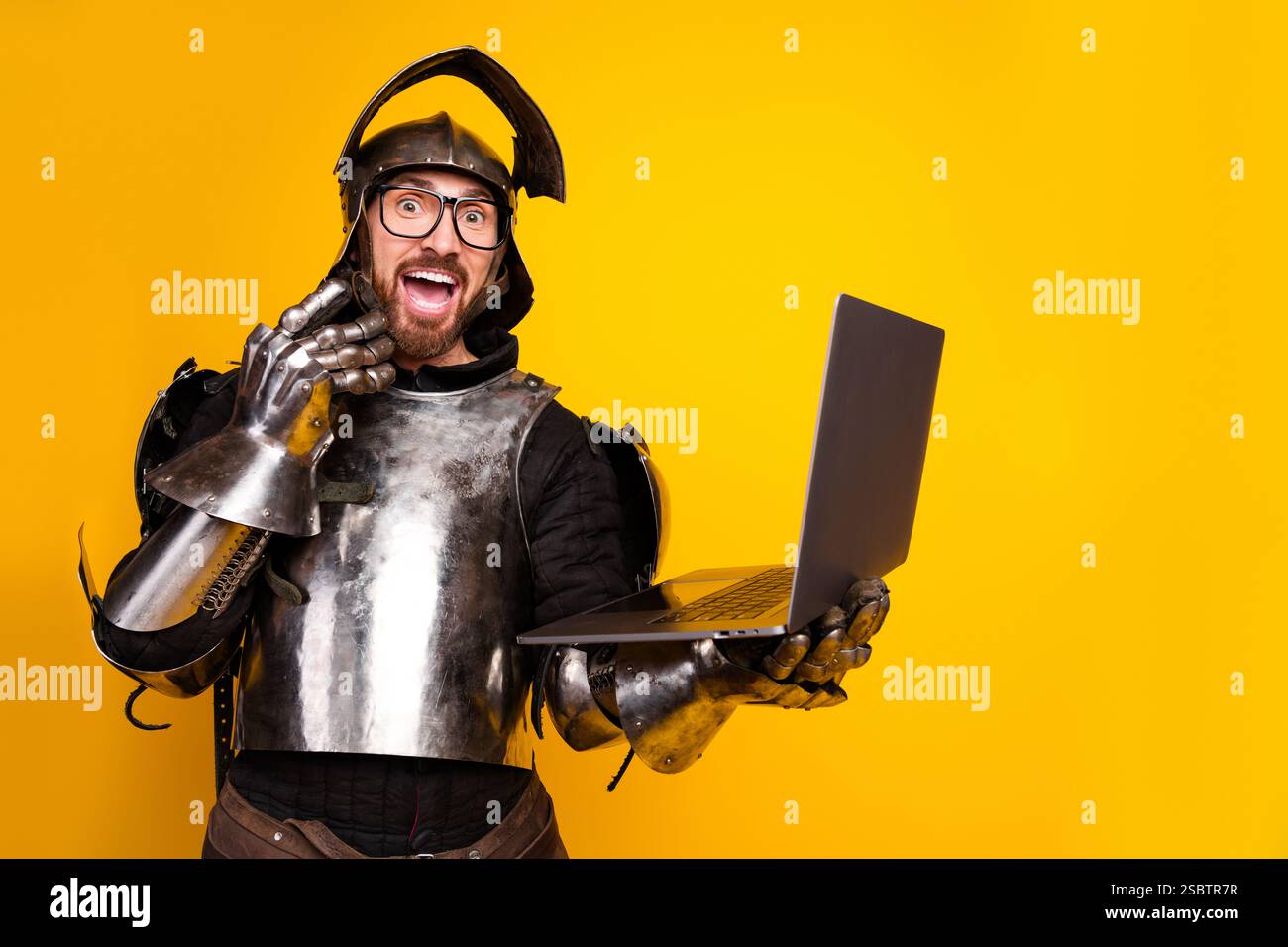 A young man in knight armor expressing surprise with a laptop against a ...