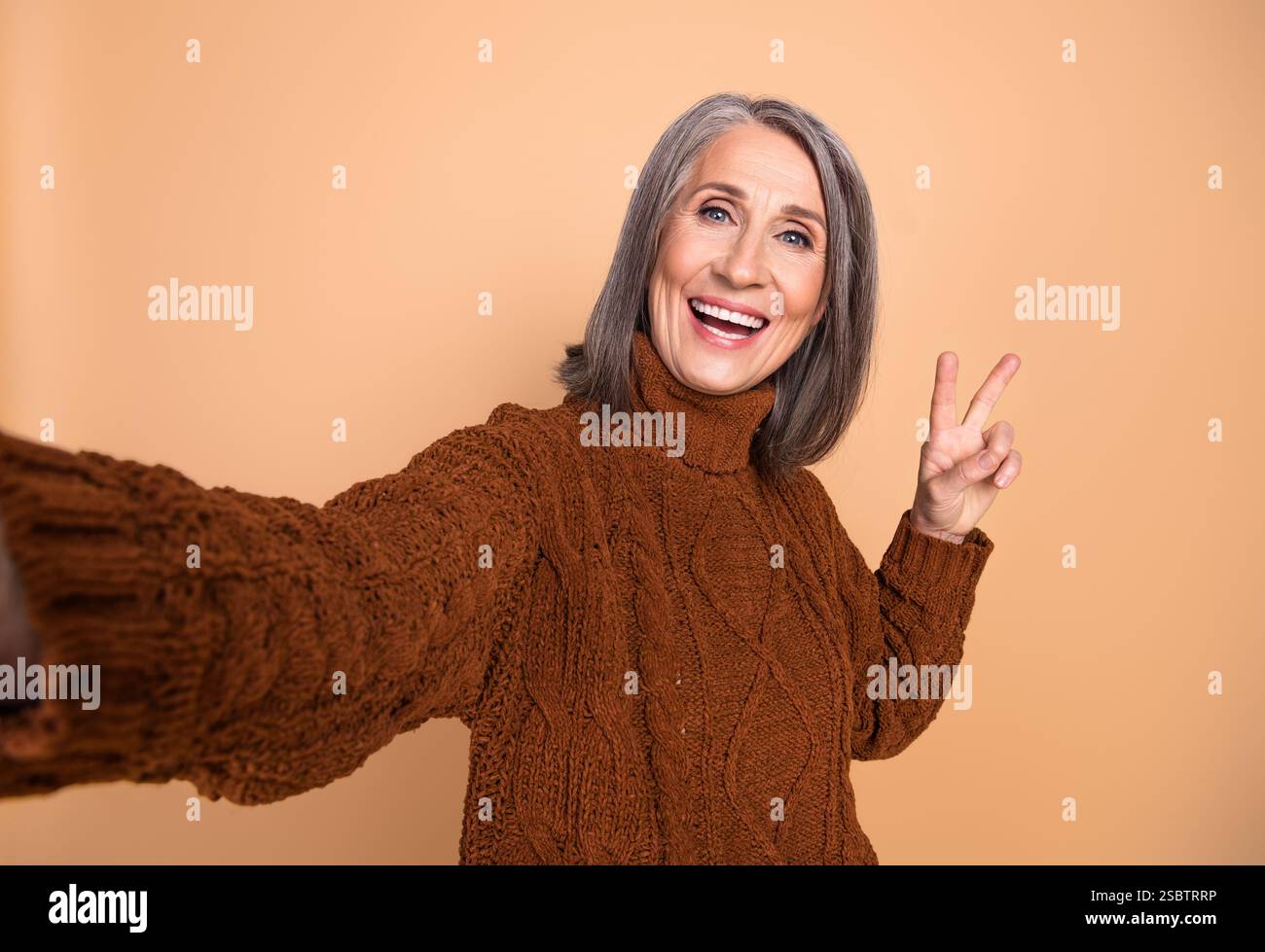 Portrait of a cheerful mature woman in a brown sweater against a beige ...