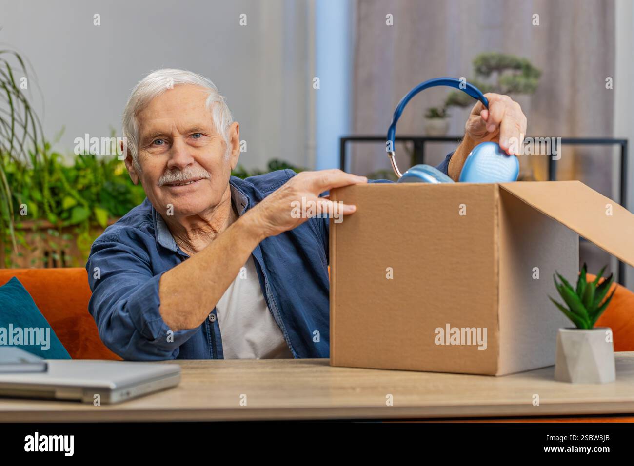 Happy senior old man unpacking delivery parcel with headphones at home ...