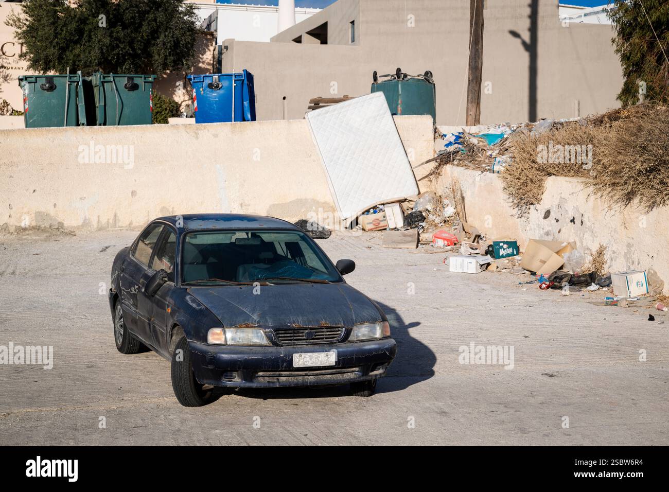 Rusty, damaged car on a gravel parking lot with garbage container and ...