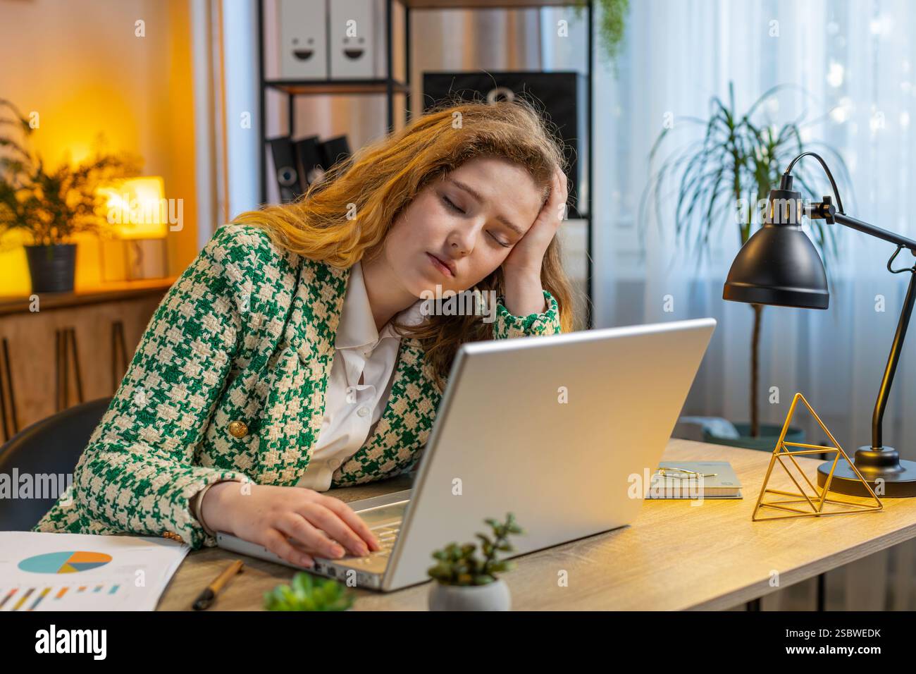Bored sleepy young blond businesswoman worker working on laptop ...