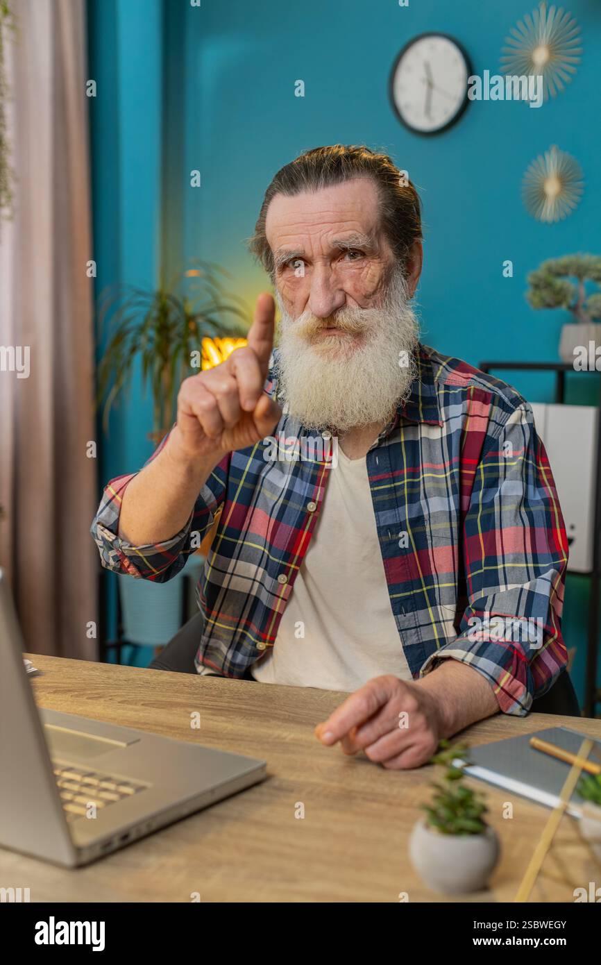 Senior man working on laptop shakes finger and saying No be careful ...