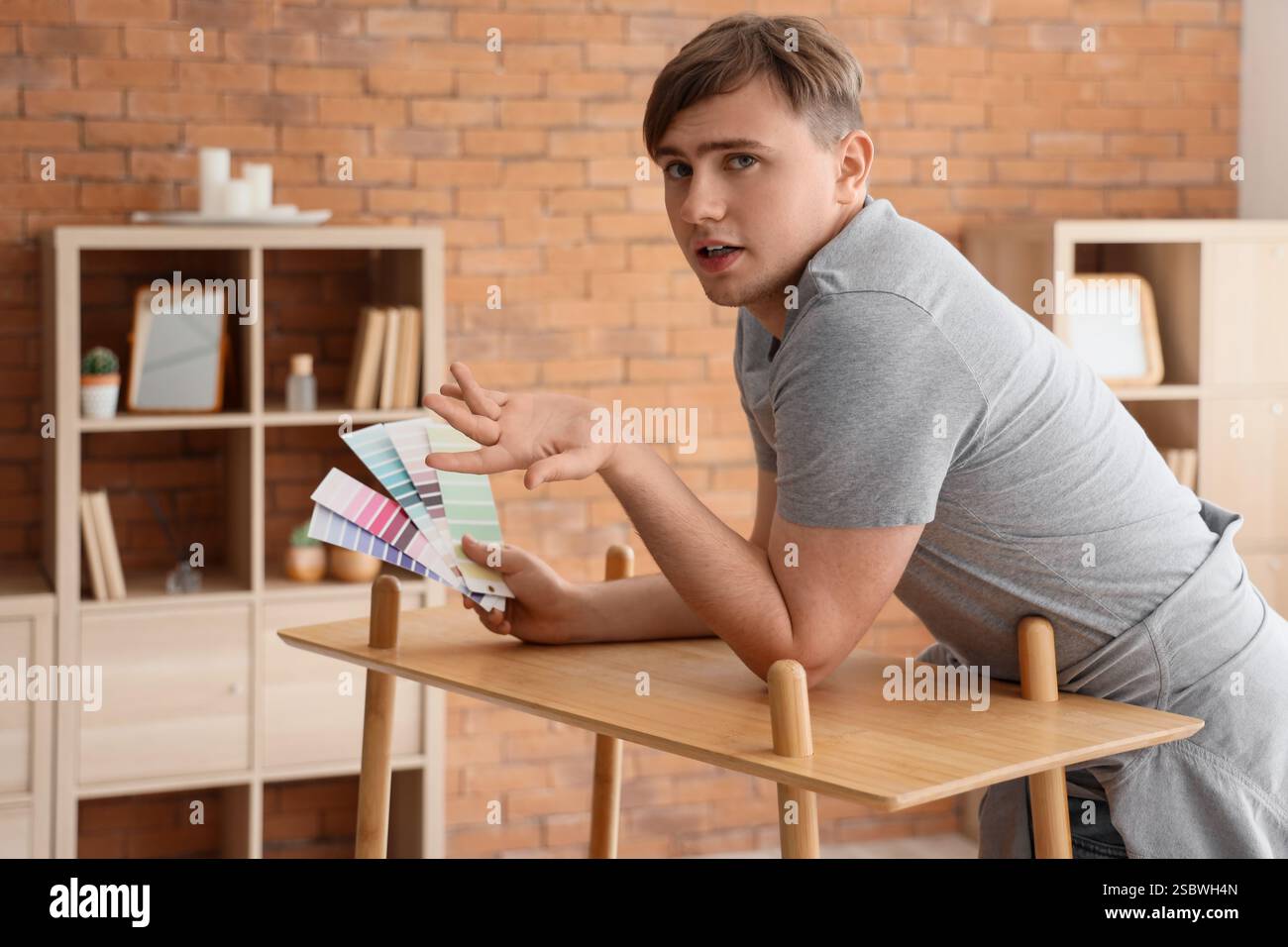 Confused young man with paint color palettes and shelf unit at home ...