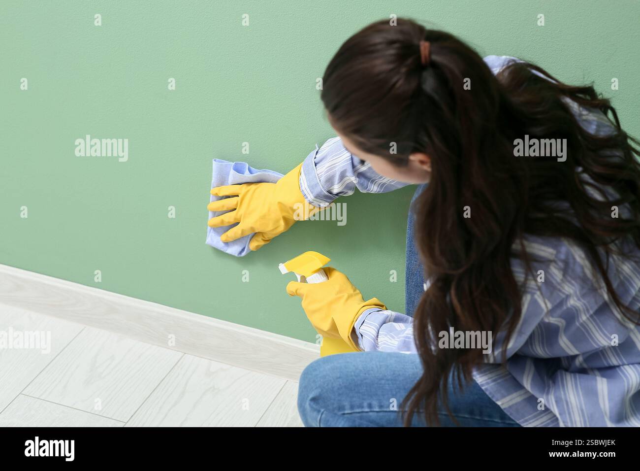 Young woman with spray bottle and rag removing mold from green wall at ...