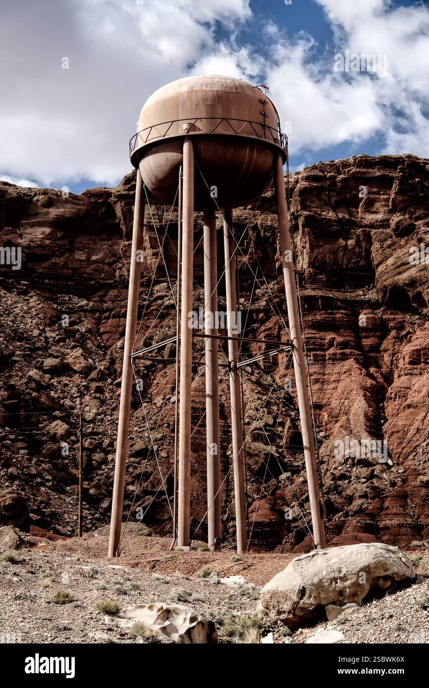 A large metal water tower is on a rocky hill. The tower is tall and has ...