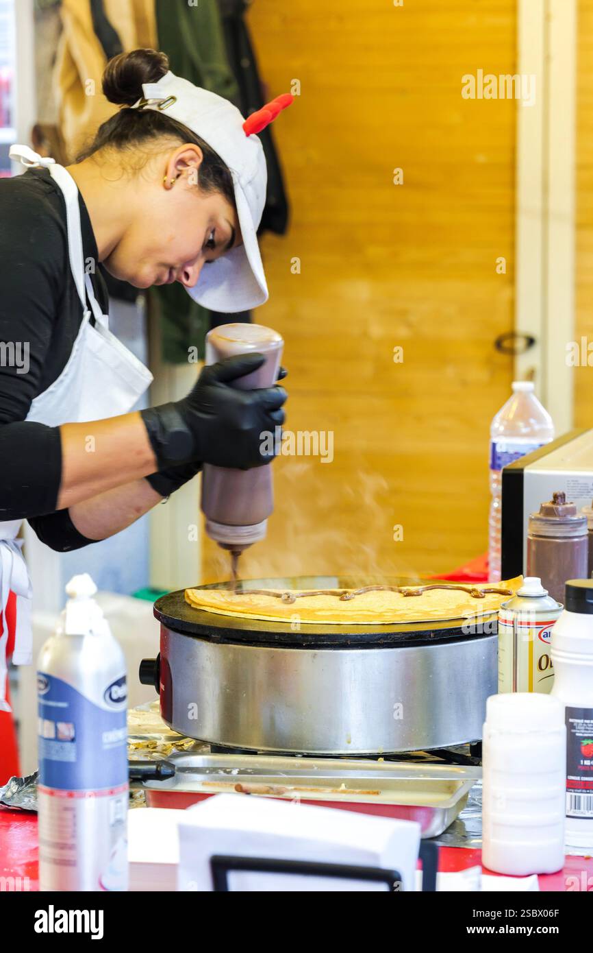 A cook preparing a crepe on an electric crepe maker at a market stall ...