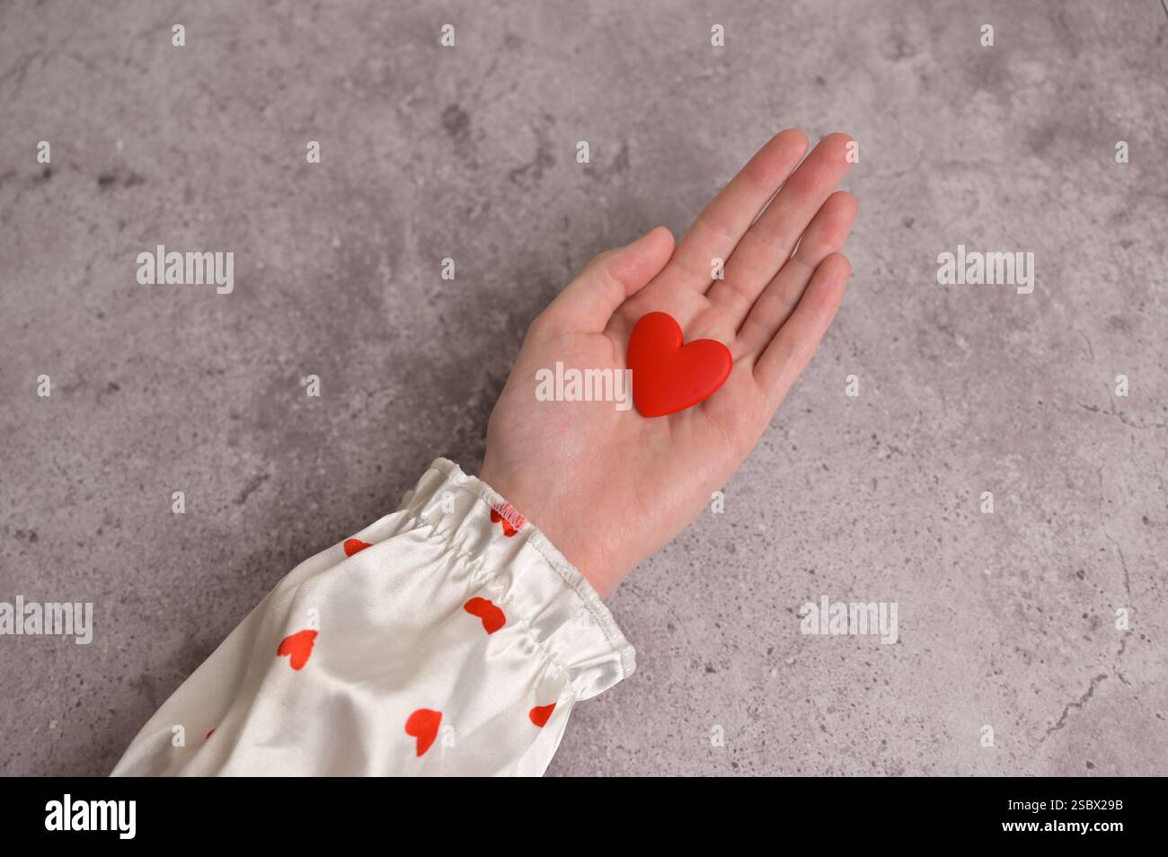 Woman holding one red earring heart shape in hand. White cloth with ...